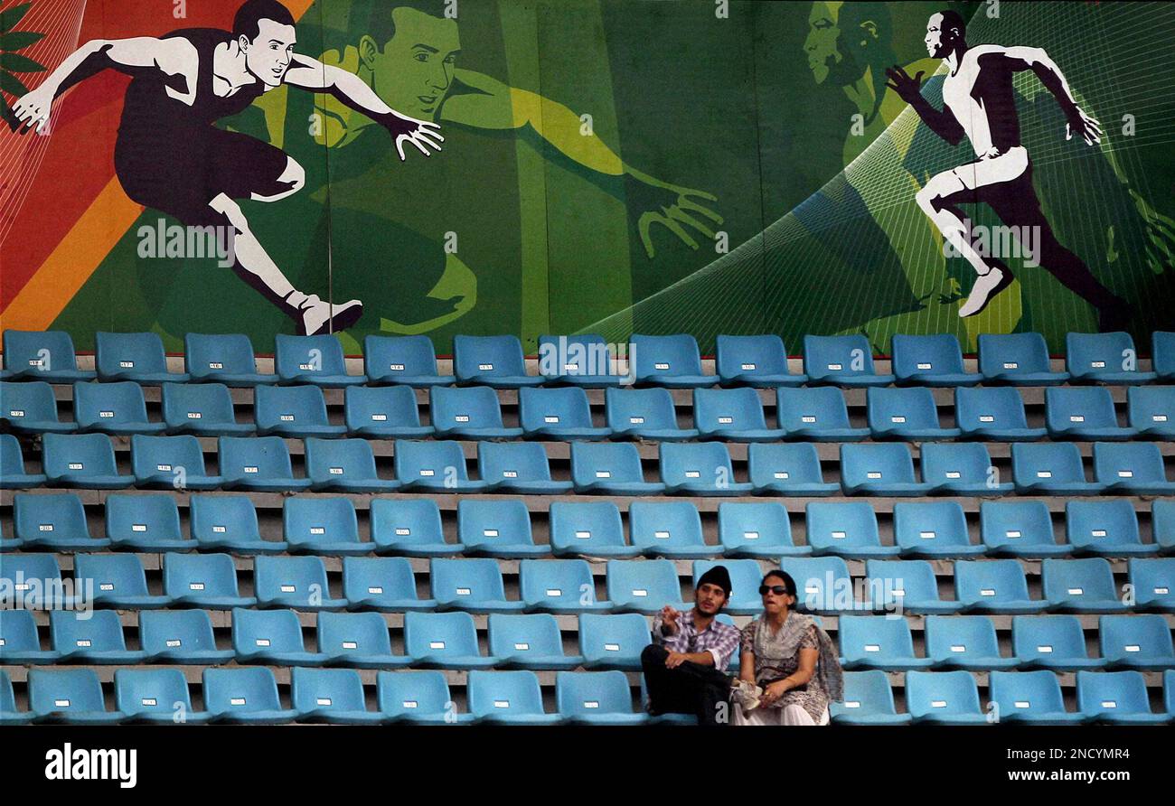 Two Indian fans watch athletics events, surrounded by unoccupied seats ...