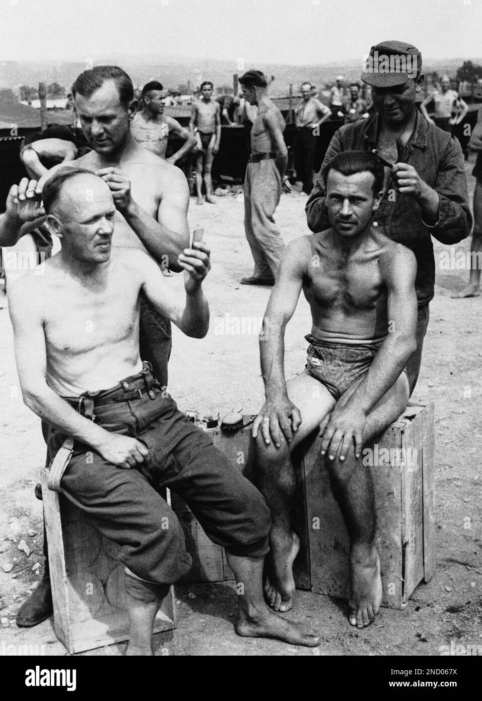 Two German POW’s, stripped to the waist are given a haircut by fellow ...
