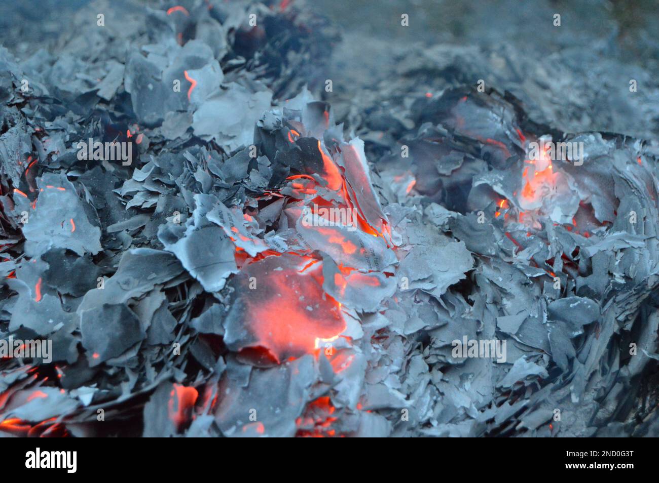 A closeup of hot red glowing embers in a dying fire under dim blue ...