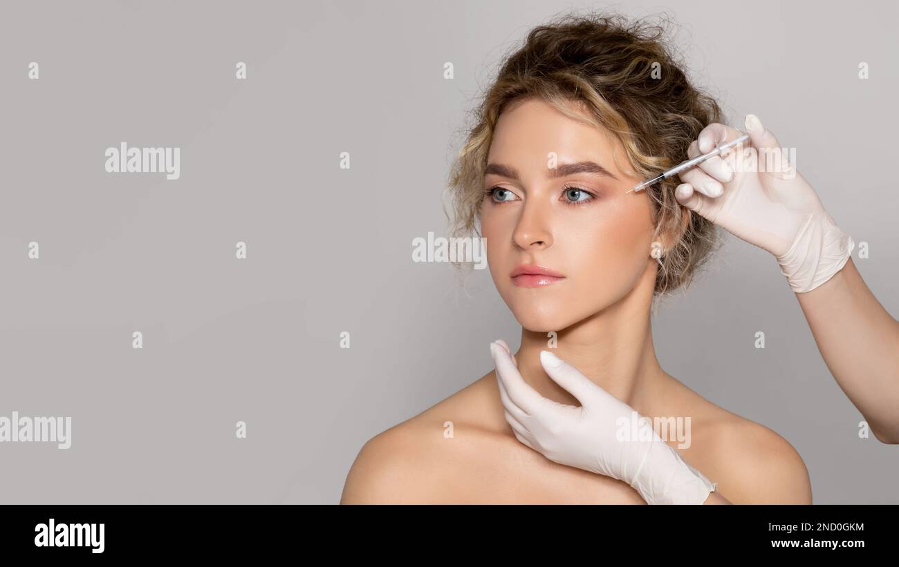 Young beautiful woman getting botox injection for eyes area, standing ...