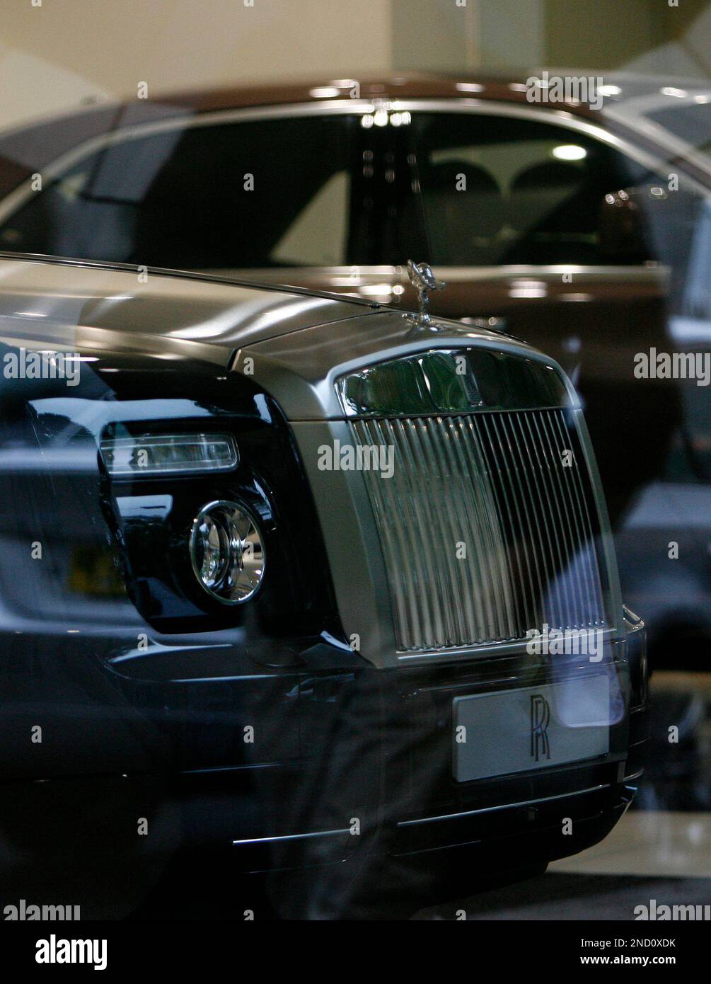 A pedestrian with an umbrella is reflected in a shop window as a Rolls ...