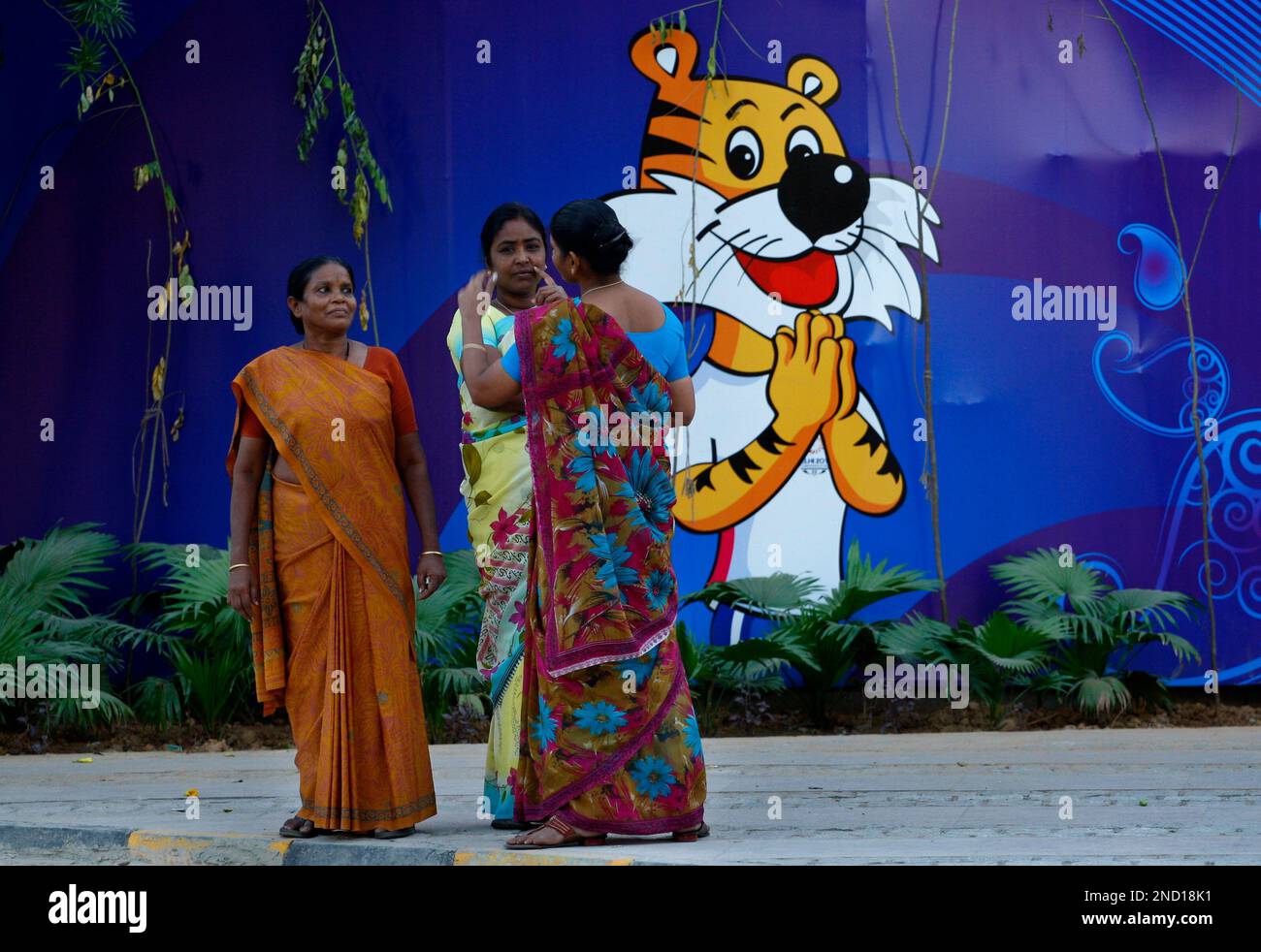 Indian women wait for transport near a portrait of Shera, the mascot of ...