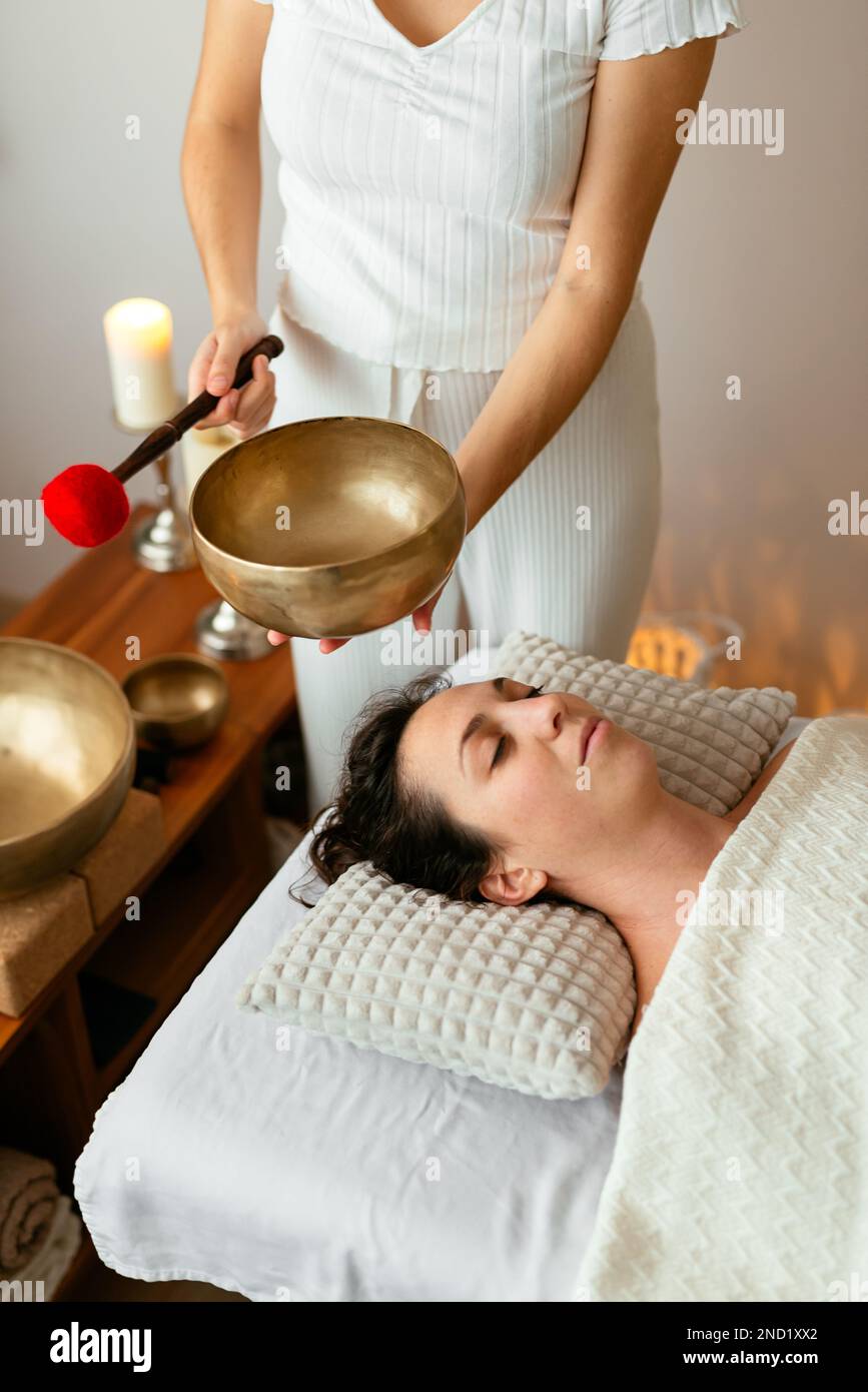 Relaxed young ethnic female client lying on massage table with closed eyes while therapist ...