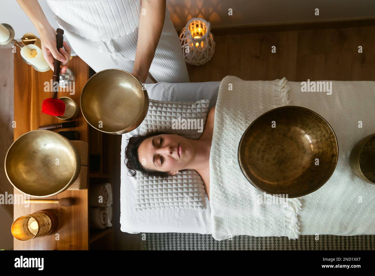 Top view of relaxed young ethnic female client lying on massage table with closed eyes while ...
