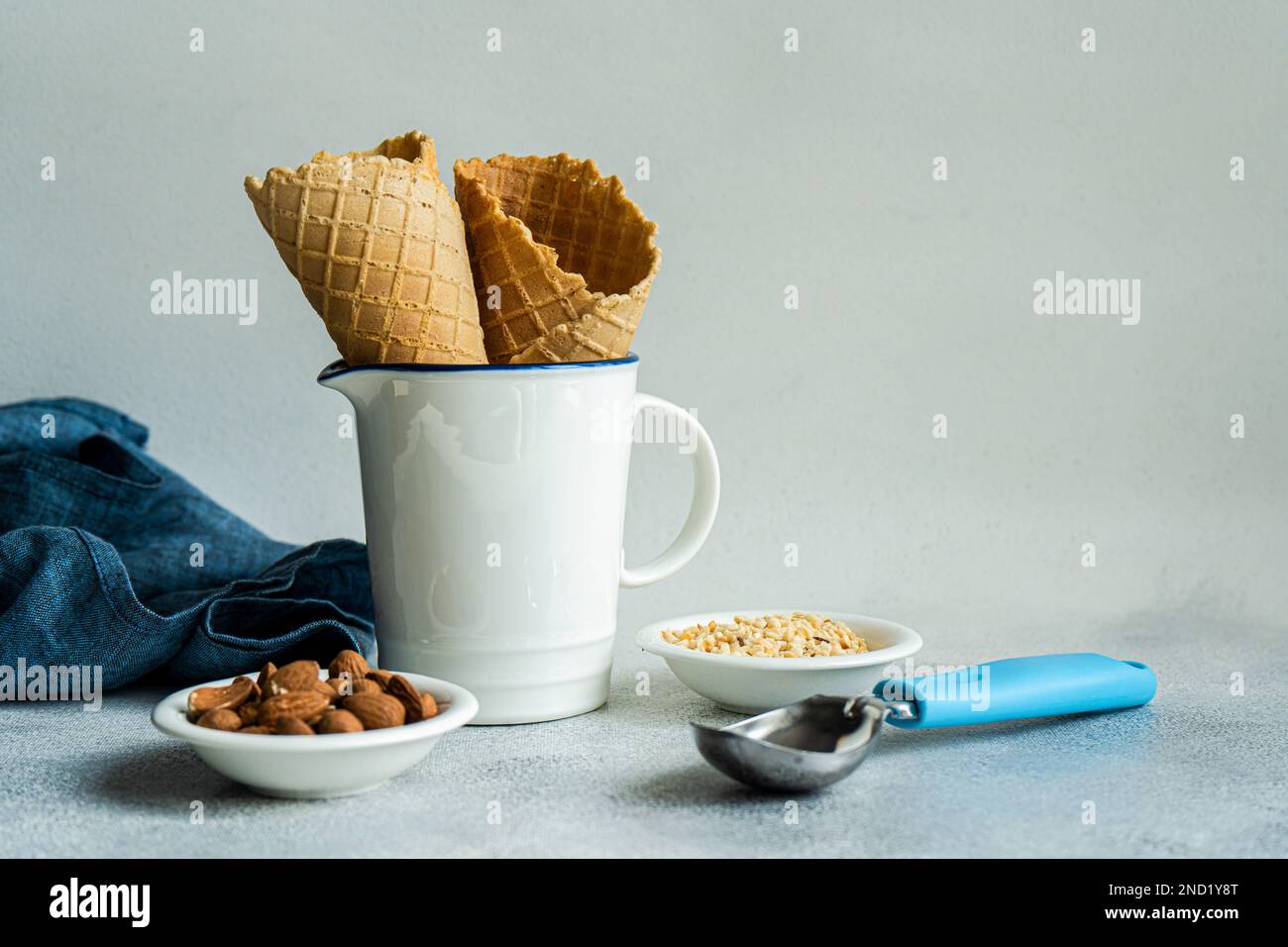 Waffle cones and nuts for ice cream preparation on concrete table with ...