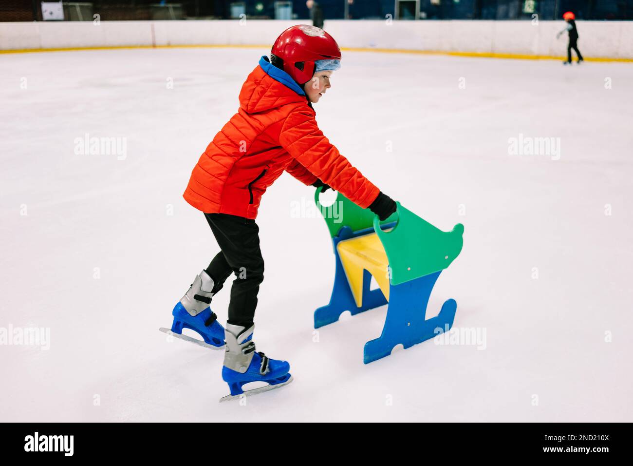 Calm boy in warm clothes and protective helmet learning ice skating ...