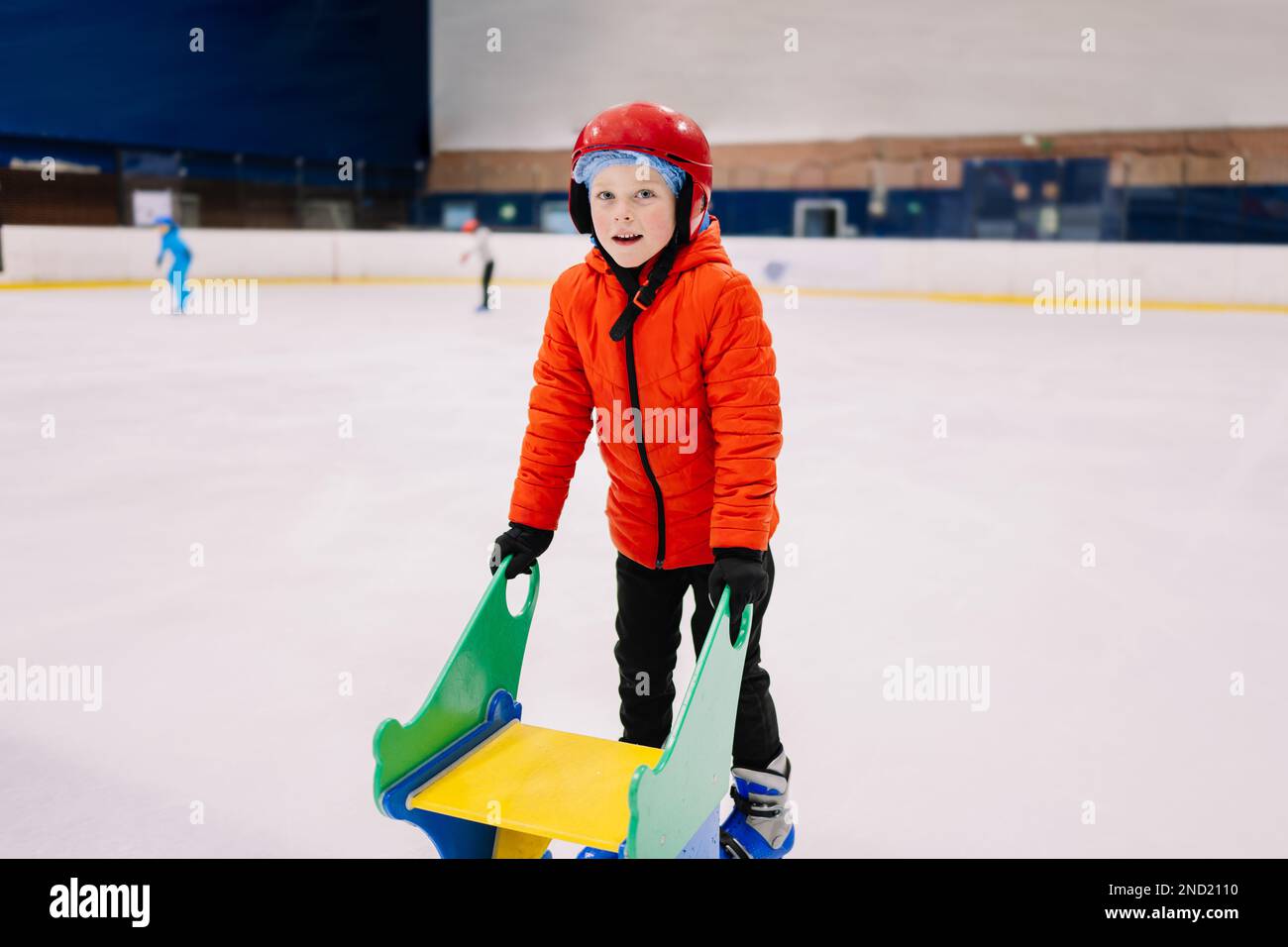 Cheerful boy in warm clothes and protective helmet learning ice skating ...