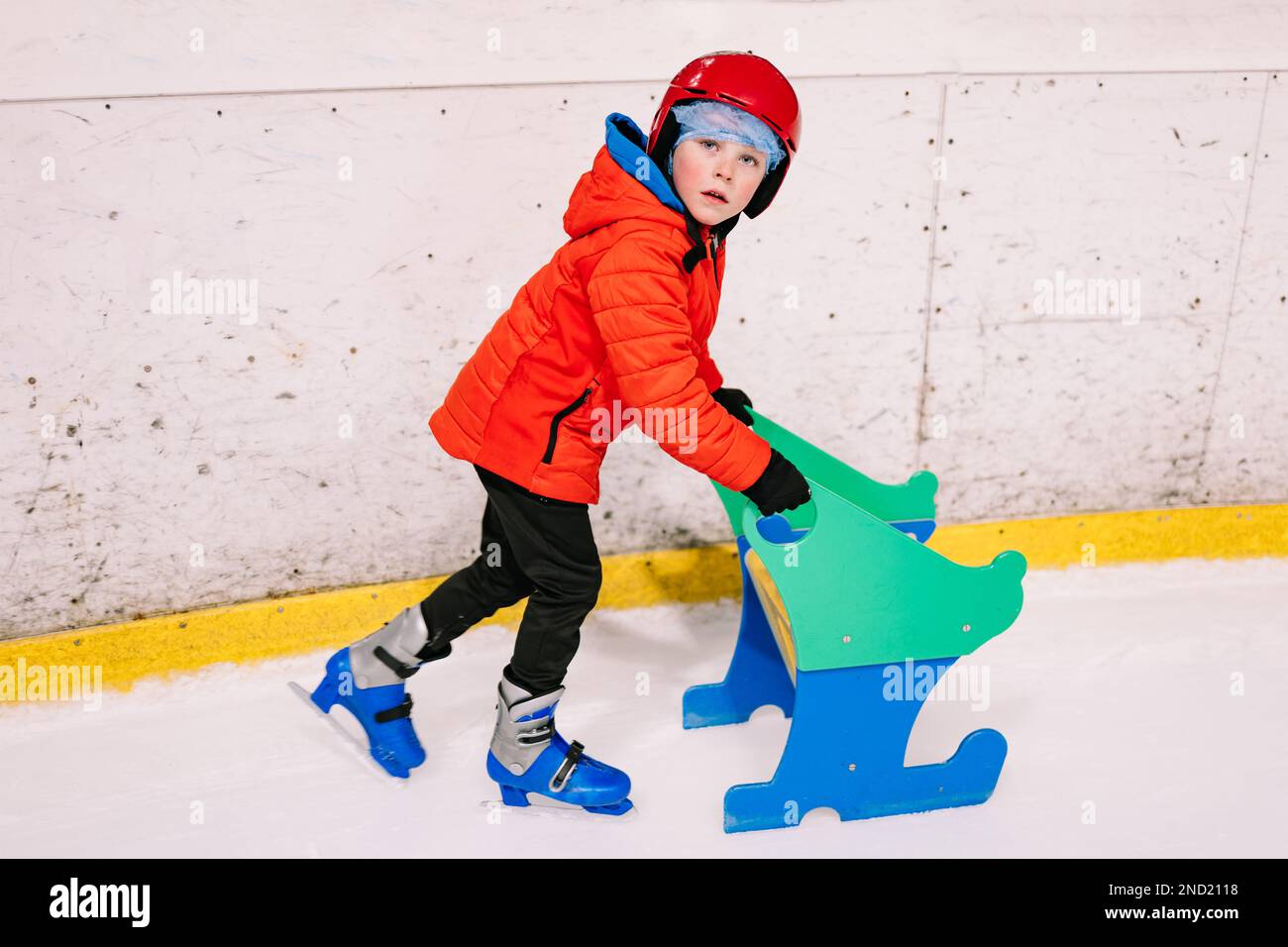 Calm boy in warm clothes and protective helmet learning ice skating ...