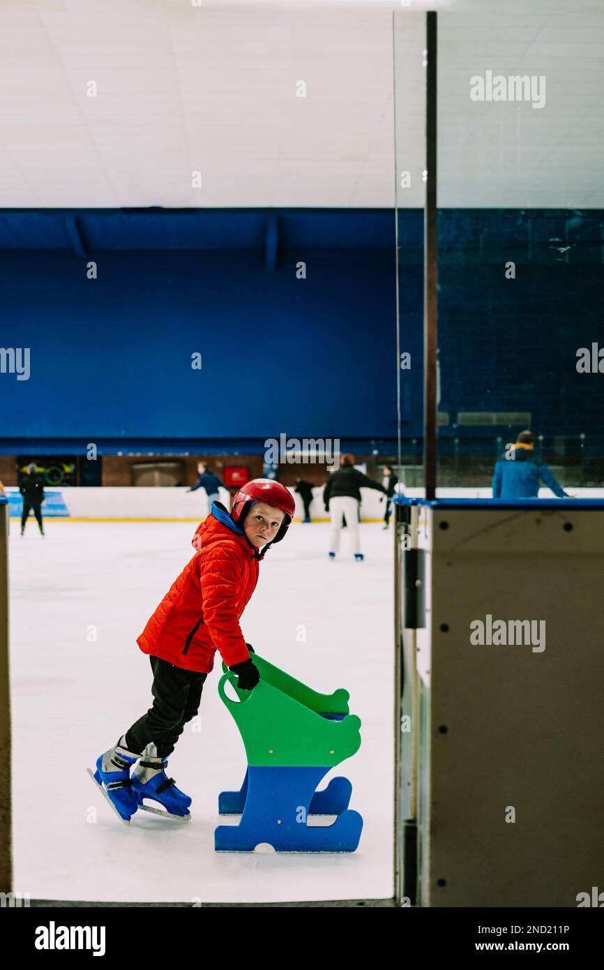Calm boy in warm clothes and protective helmet learning ice skating ...