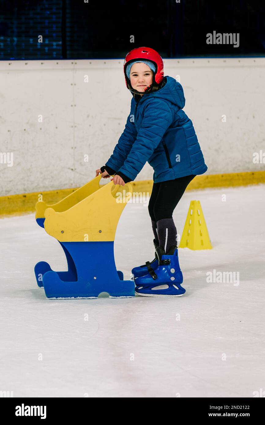 Positive girl in warm clothes and protective helmet learning ice ...