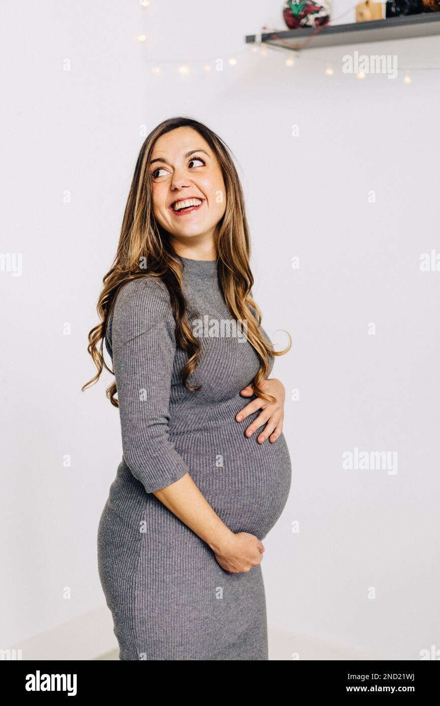 Positive young female with wavy hair in gray knitted dress smiling and ...
