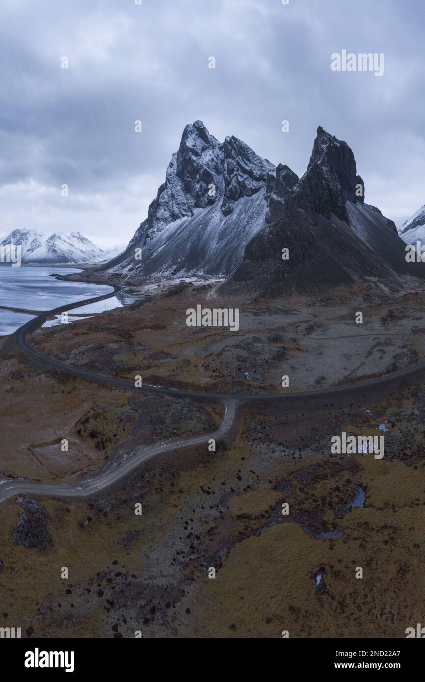 Aerial view of asphalt road going between snowy mountain and blue ocean ...