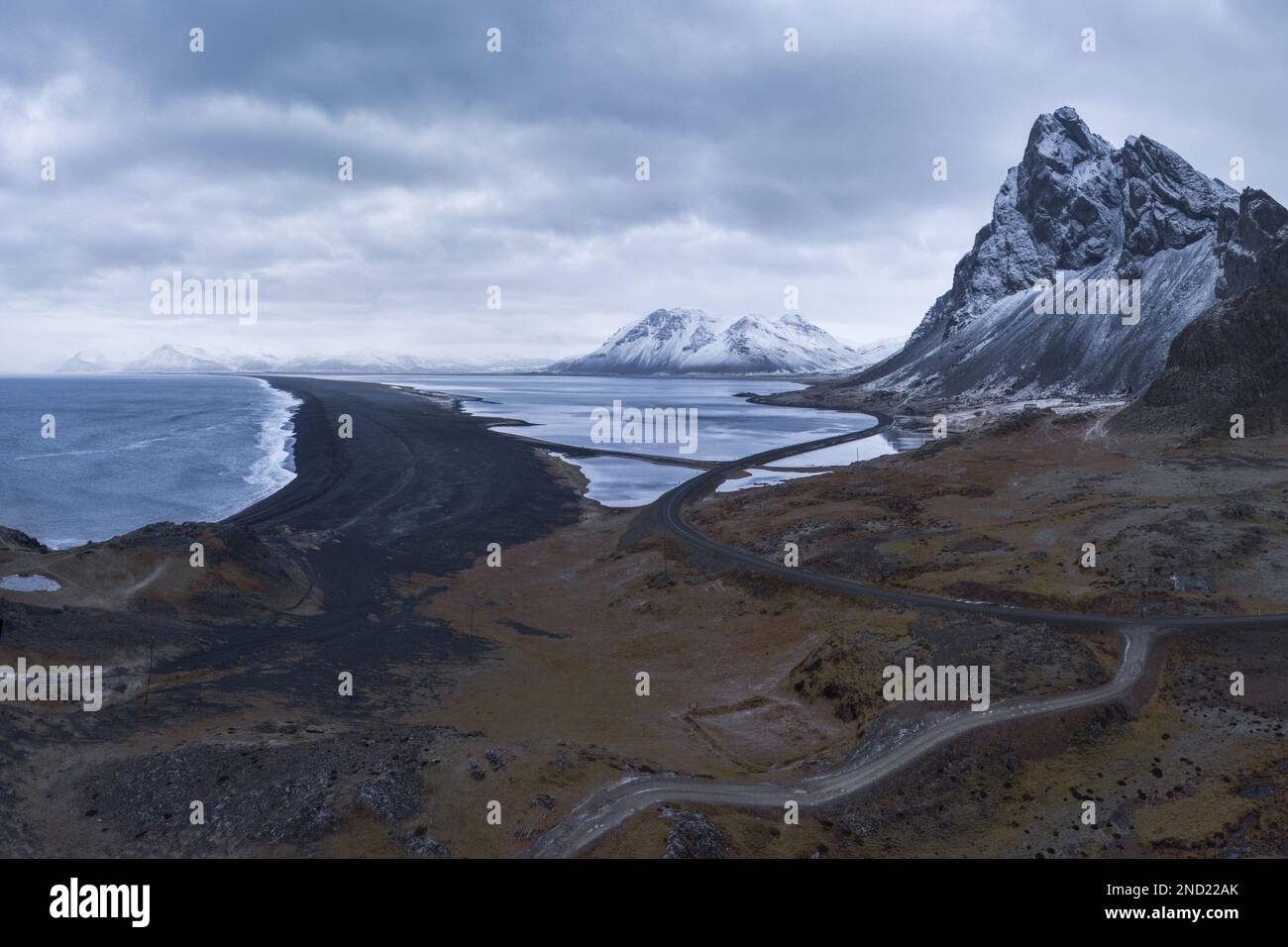 Aerial view of asphalt road going between snowy mountain and blue ocean ...