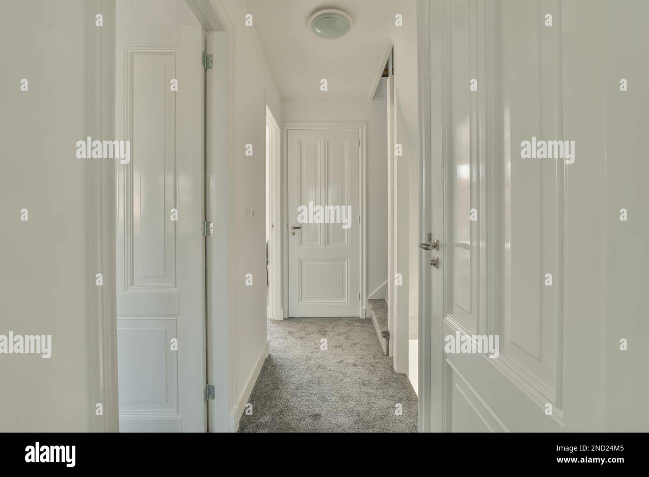 Narrow corridor with white walls and doors leading to rooms in modern ...