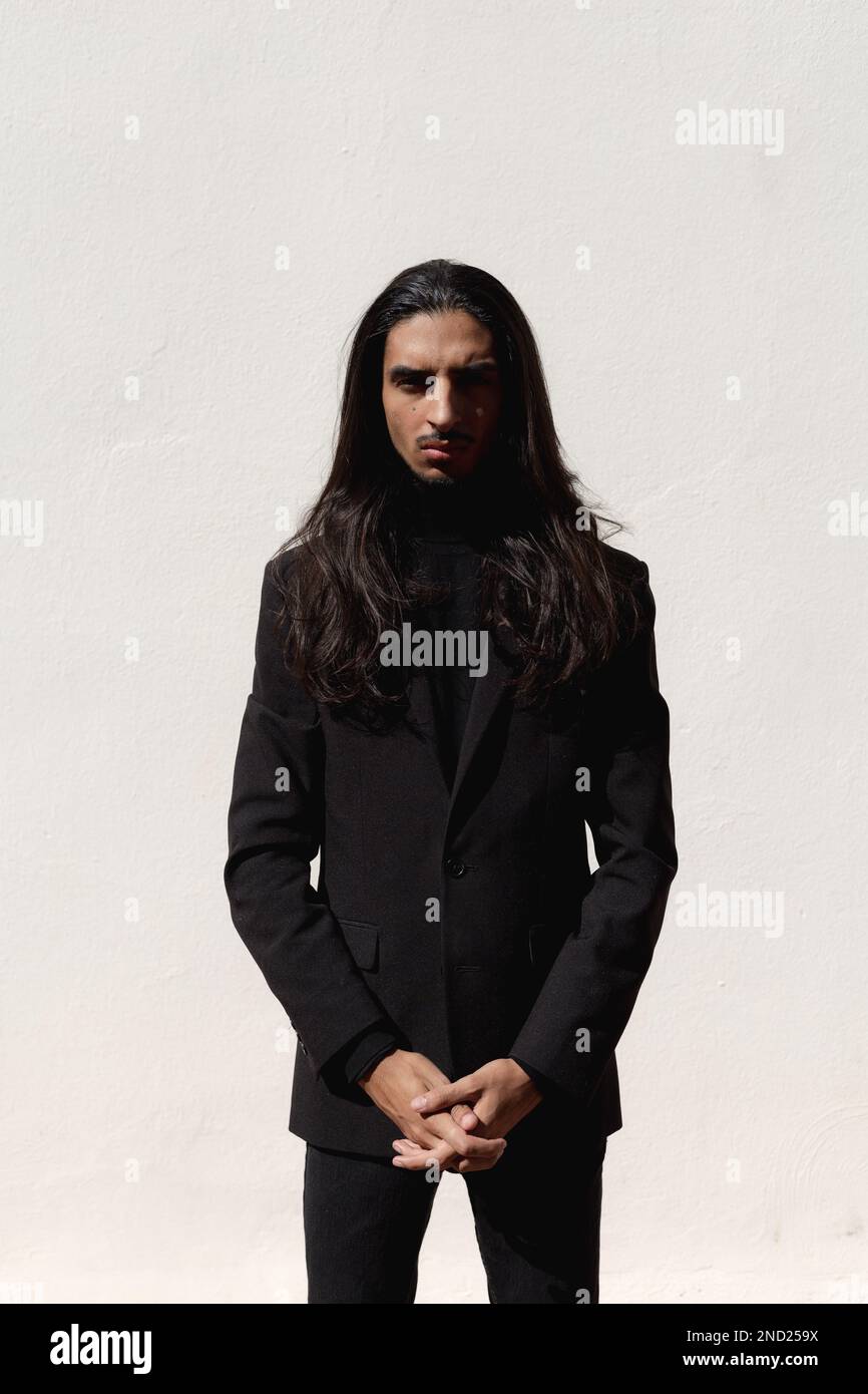 Confident young Hispanic male model with long dark hair wearing black ...