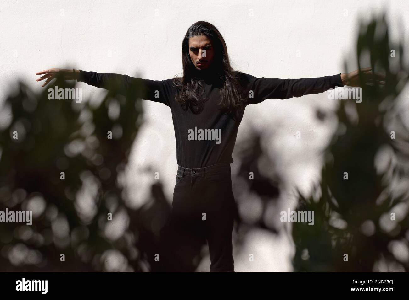 Calm Hispanic male model with long hair in black outfit standing ...