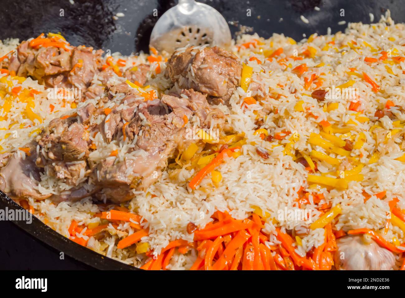 Process of cooking pilaf in huge cauldron at summer outdoor food market ...