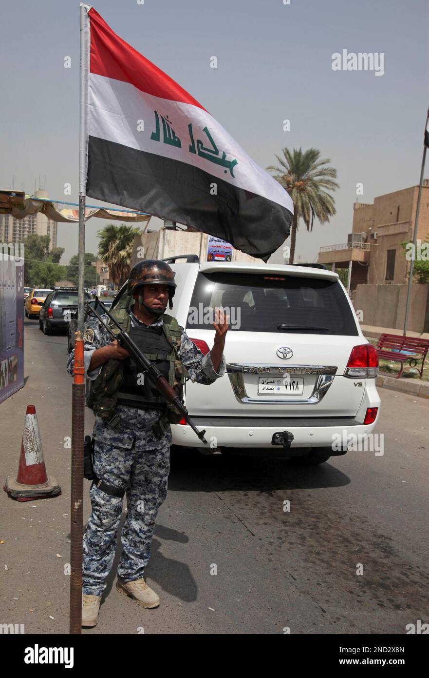 An Iraqi police officer stands guard next to the Iraqi flag at a ...