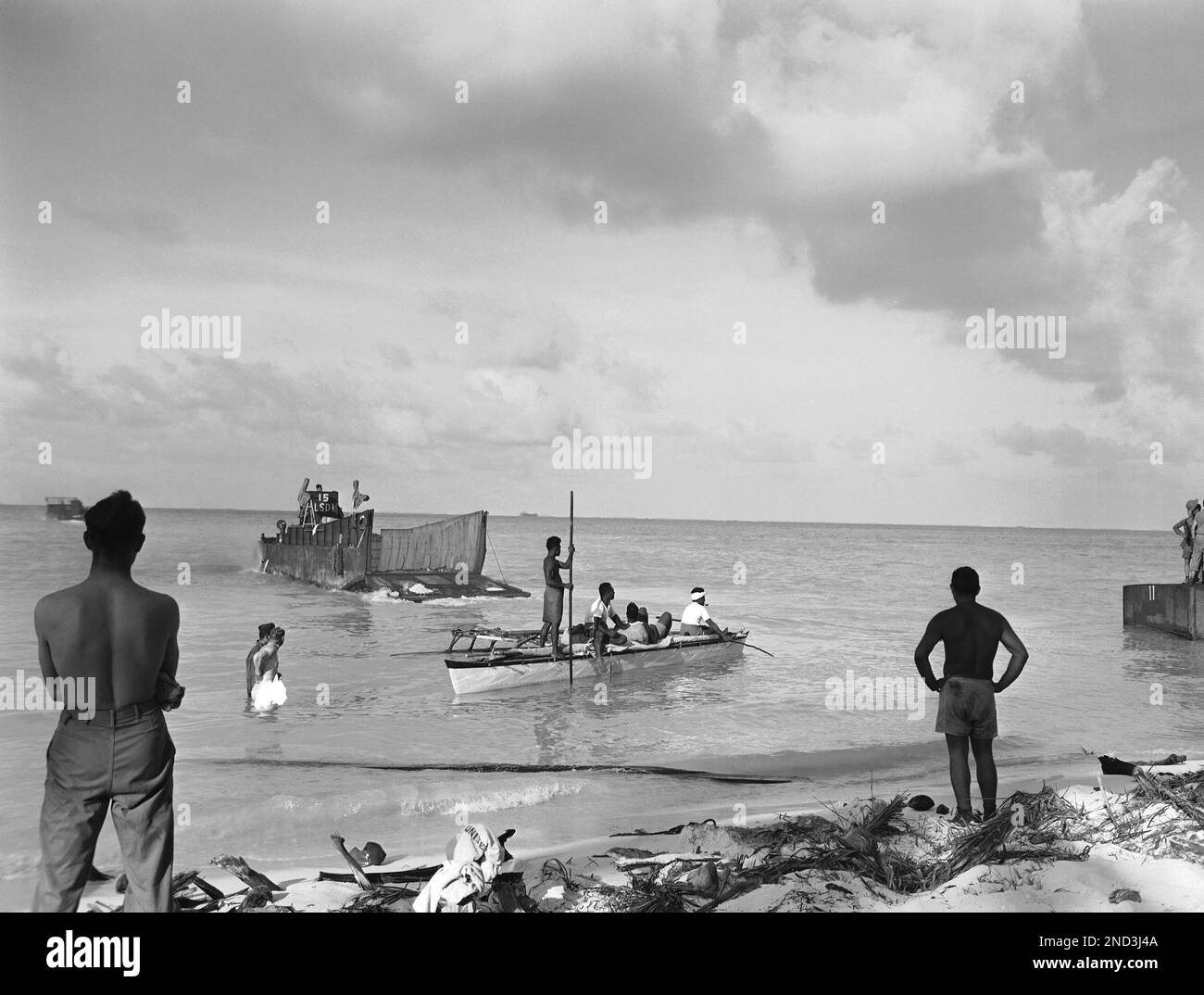 Gilbert Island natives in a canoe watch a Navy landing barge come in ...