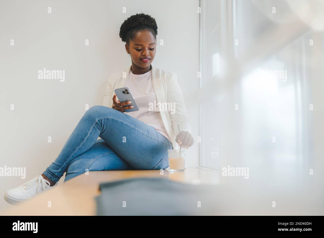 An afro woman holding and using smart phone while drinking iced coffee ...