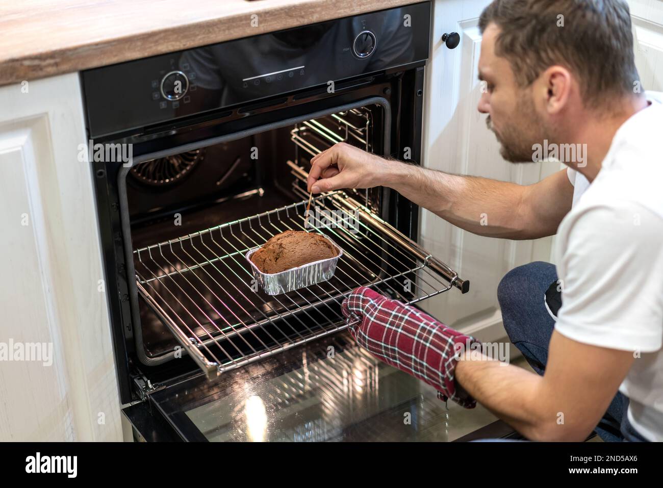 Man cooking chocolade cake at home checking readiness of baking with ...