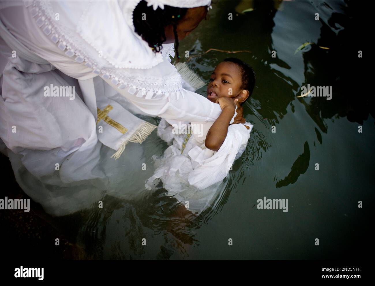 A Christian child is baptized during a mass baptism in the Jordan River ...