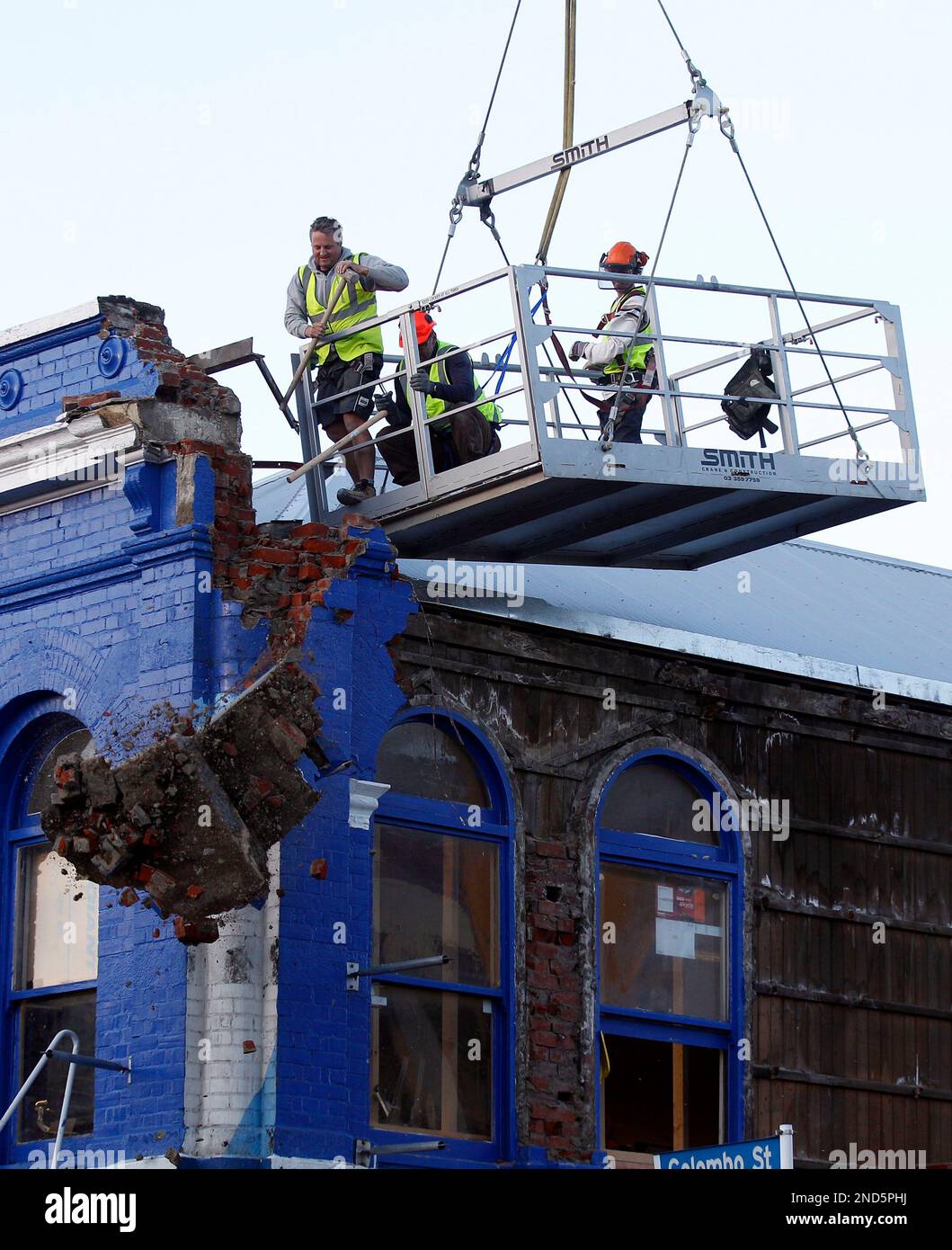 Workers push over dangerous bricks from a damaged building in ...