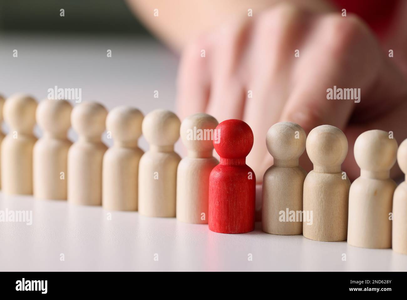 Red wooden figure in a number of white figures in a row Stock Photo - Alamy