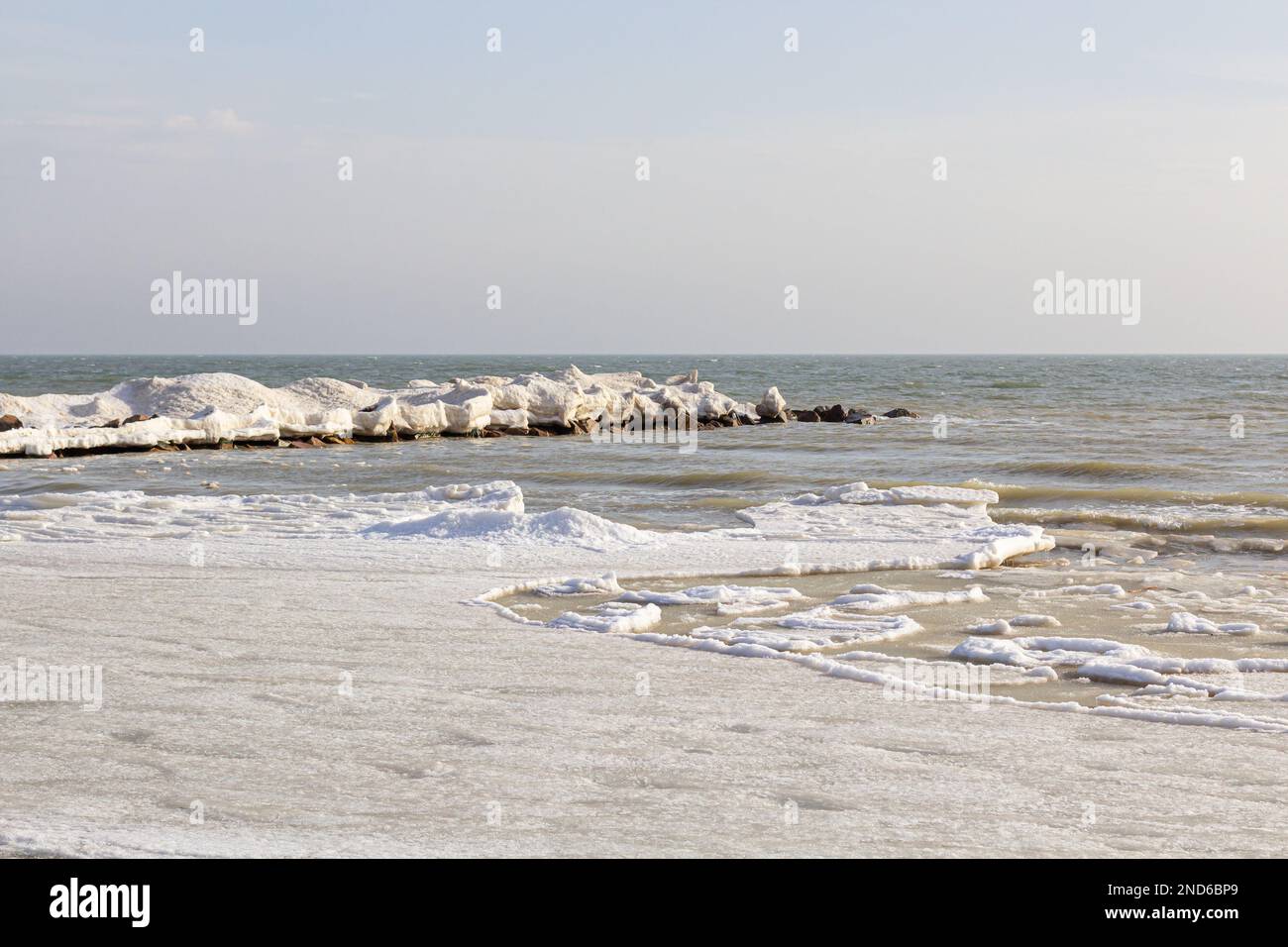 Close-up of the icy seashore, frozen waves, rocks and sun glare on the ...