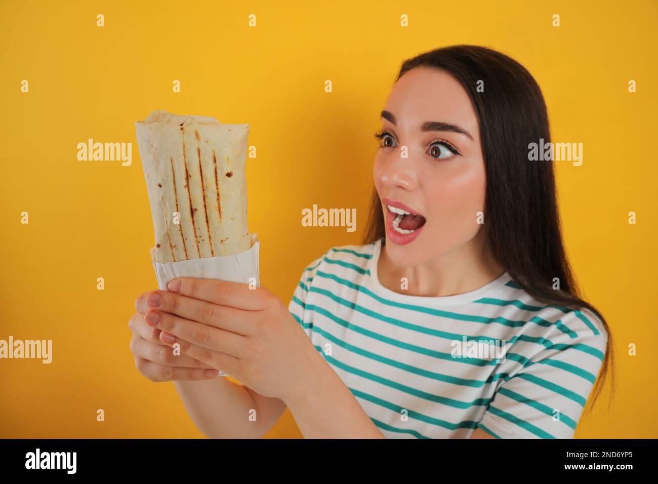 Emotional young woman holding tasty shawarma on yellow background Stock ...