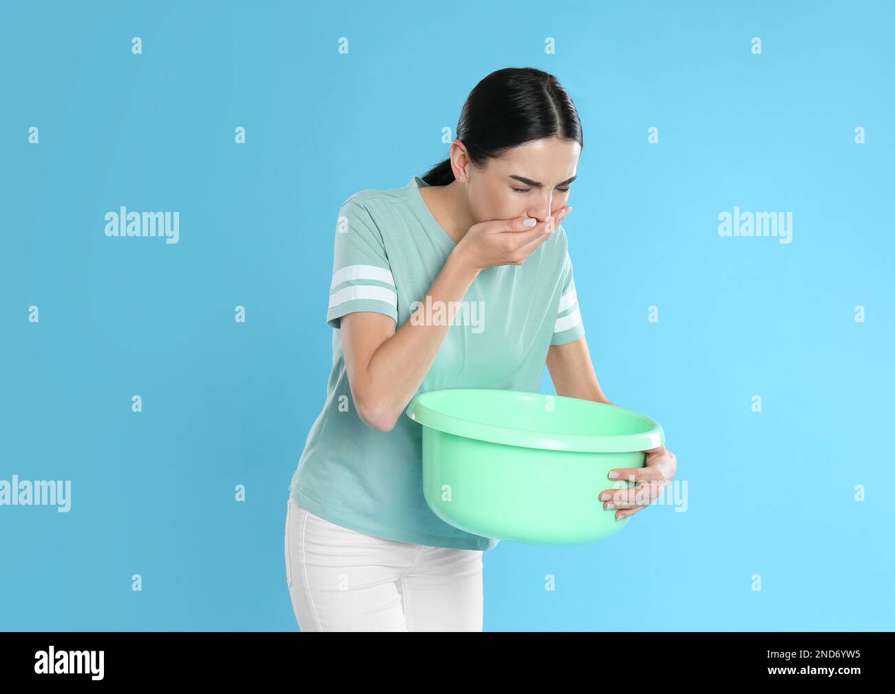 Woman with basin suffering from nausea on light blue background. Food ...