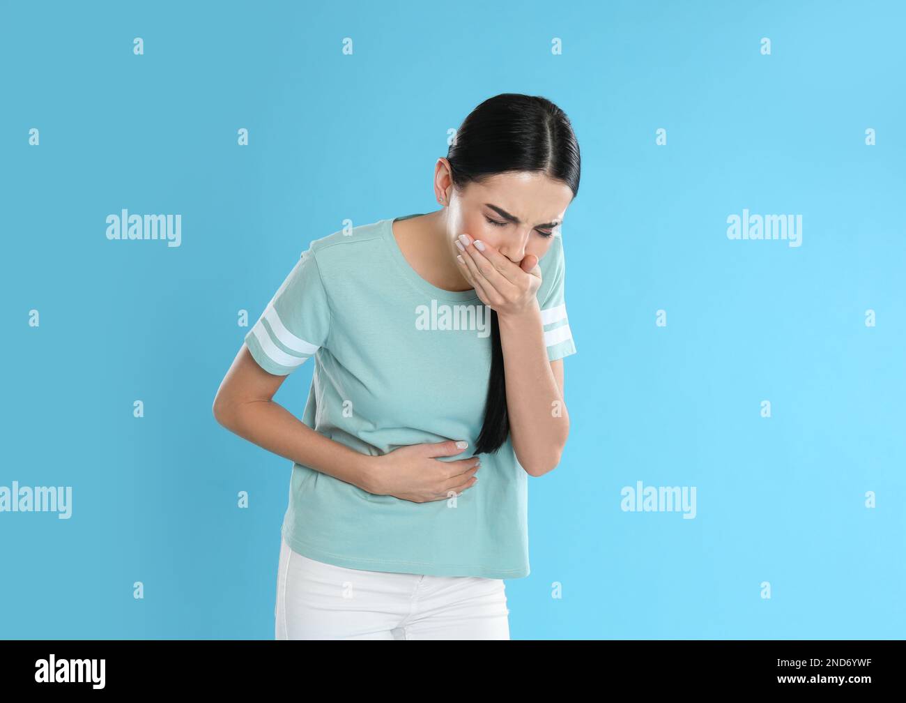 Woman suffering from stomach ache and nausea on light blue background ...