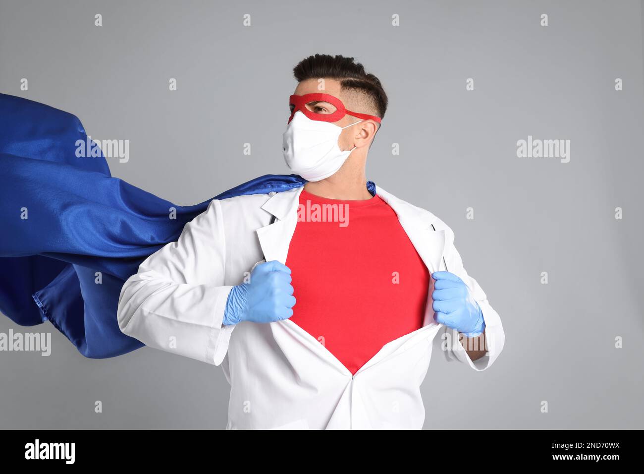 Doctor wearing face mask and cape on grey background. Super hero power ...