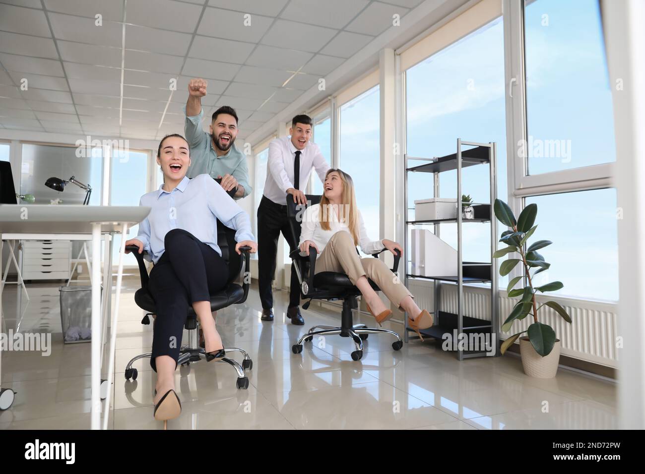 Happy office employees riding chairs at workplace Stock Photo - Alamy