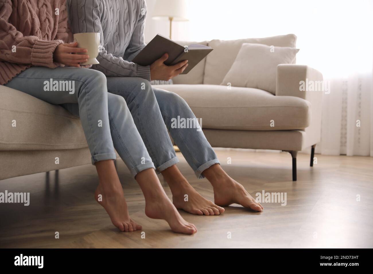 Barefoot couple sitting on sofa in living room, closeup. Floor heating ...