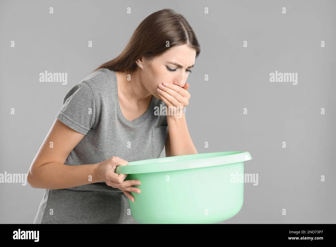 Woman with basin suffering from nausea on grey background. Food ...