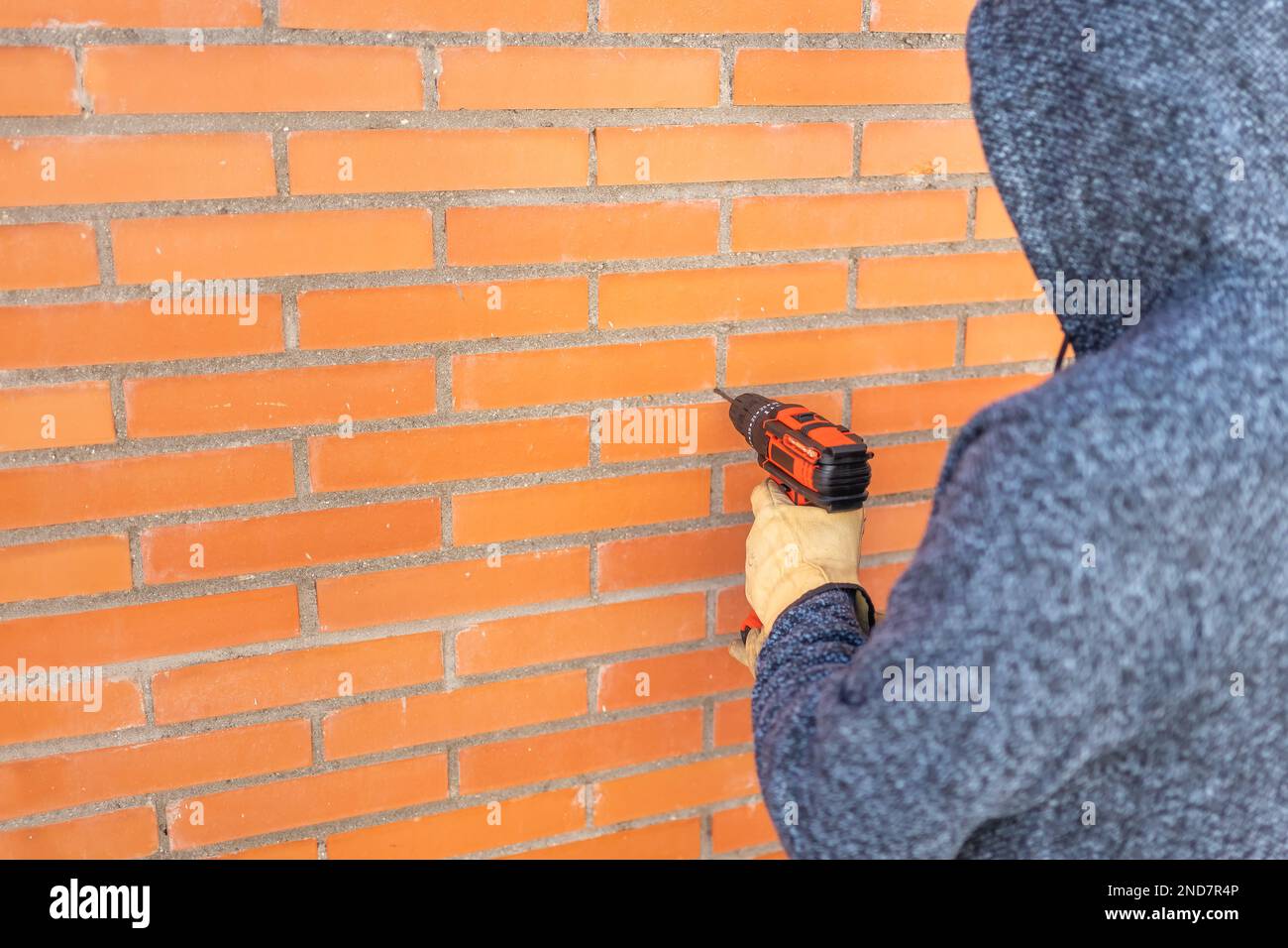 Man on his back making holes with an electric drill in the brick wall ...