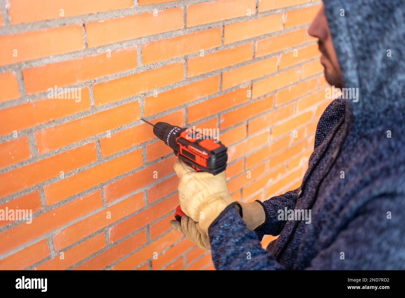 Man on his back making holes with an electric drill in the brick wall ...