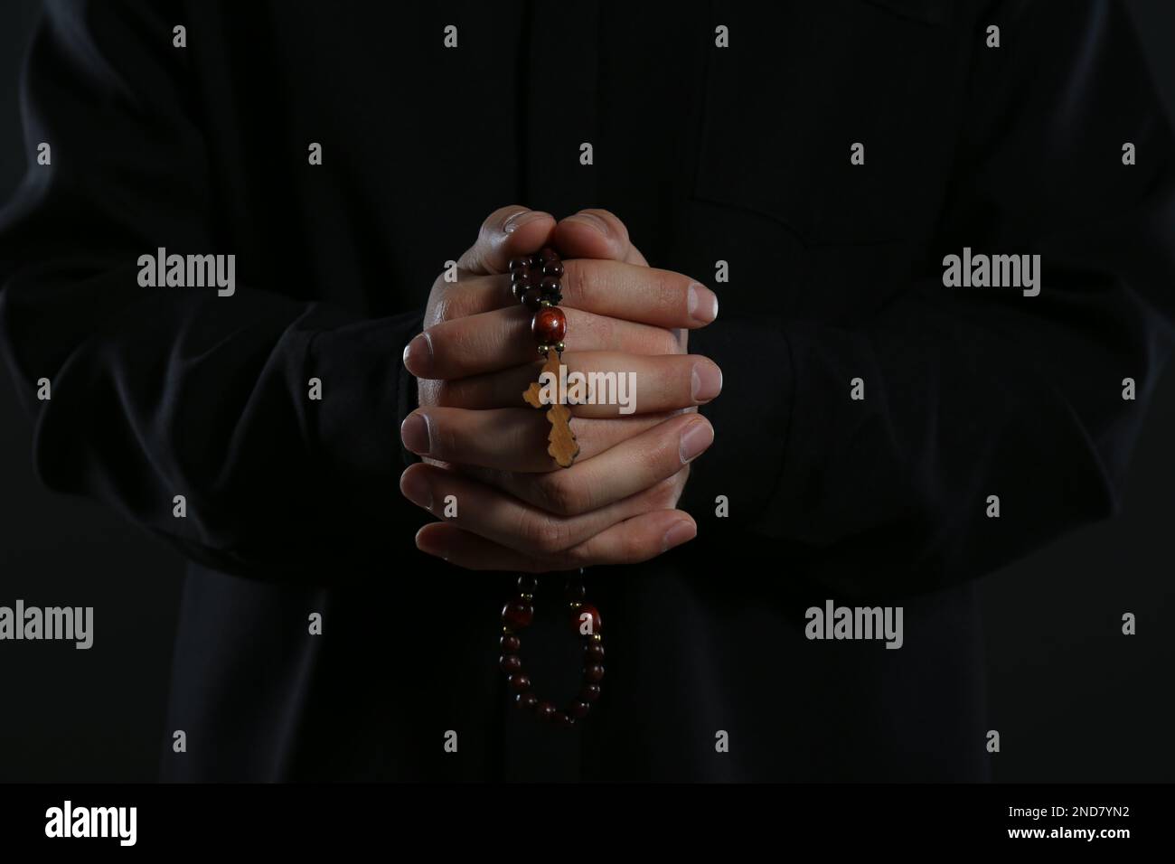 Priest with rosary beads praying on black background, closeup Stock ...