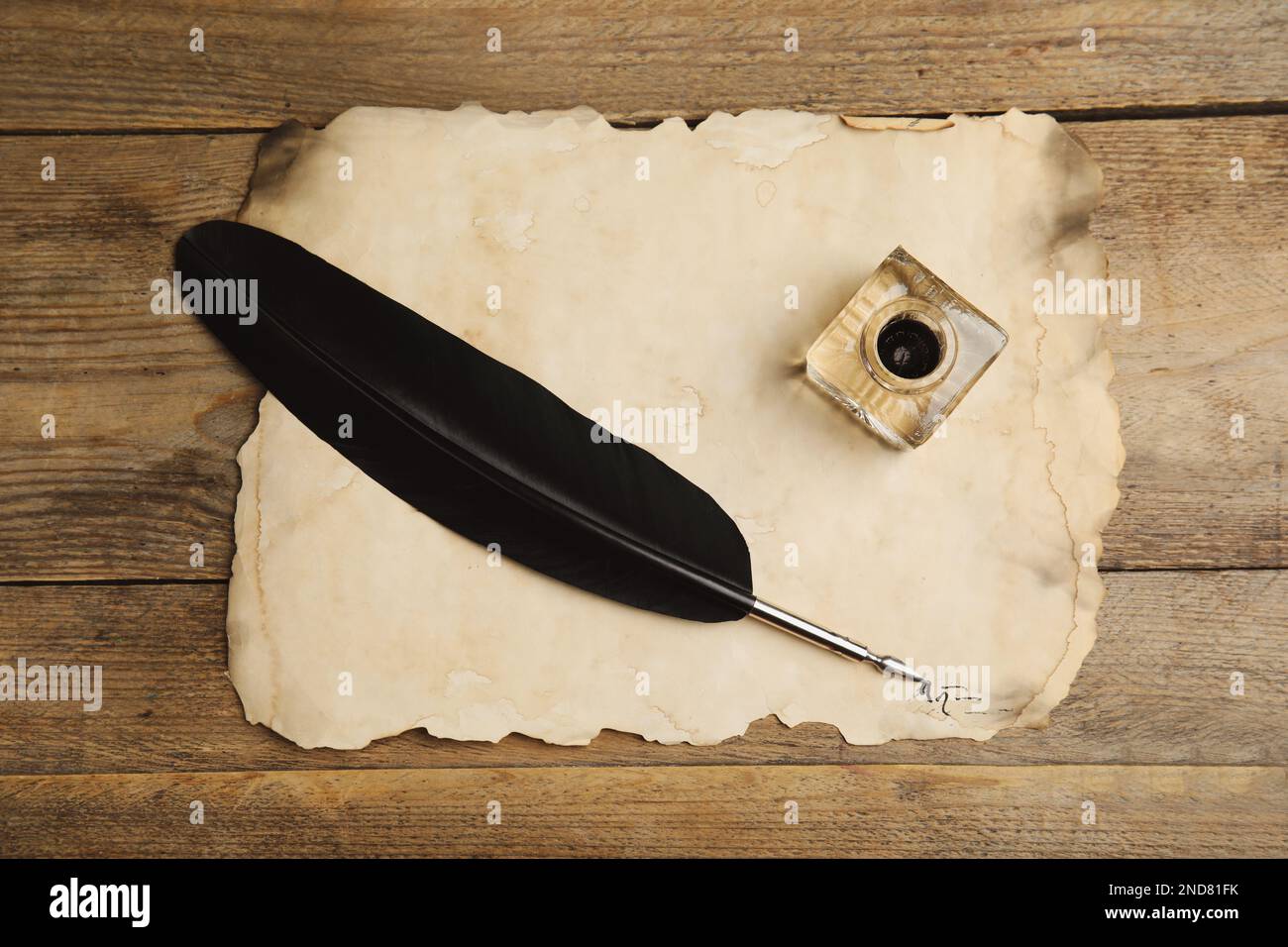 Feather pen, inkwell and parchment on wooden table, top view Stock ...