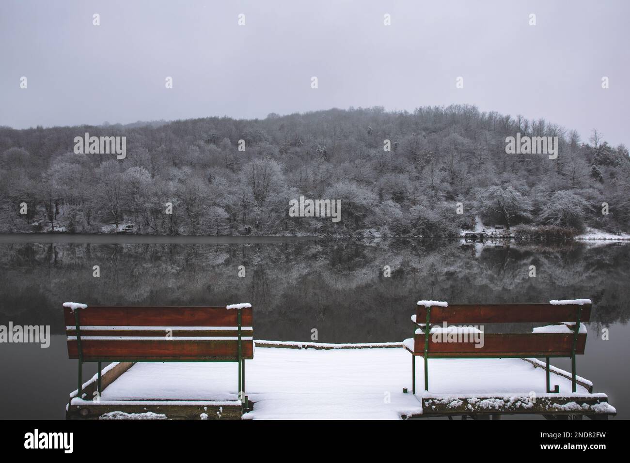 Snowy pier with two benches, winter lake shore with water reflection ...