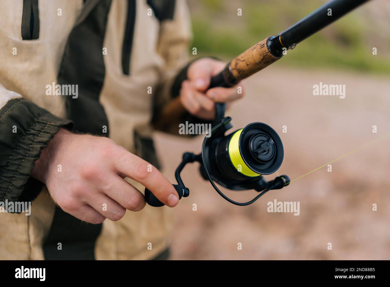 Close-up hands of unrecognizable fisherman spins reel on spinning rod ...