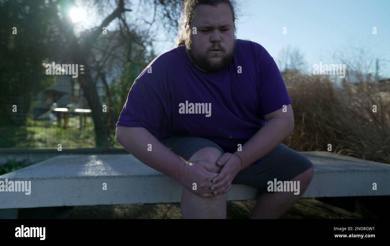 Person suffering from knee pain sitting at bench outdoors. One ...