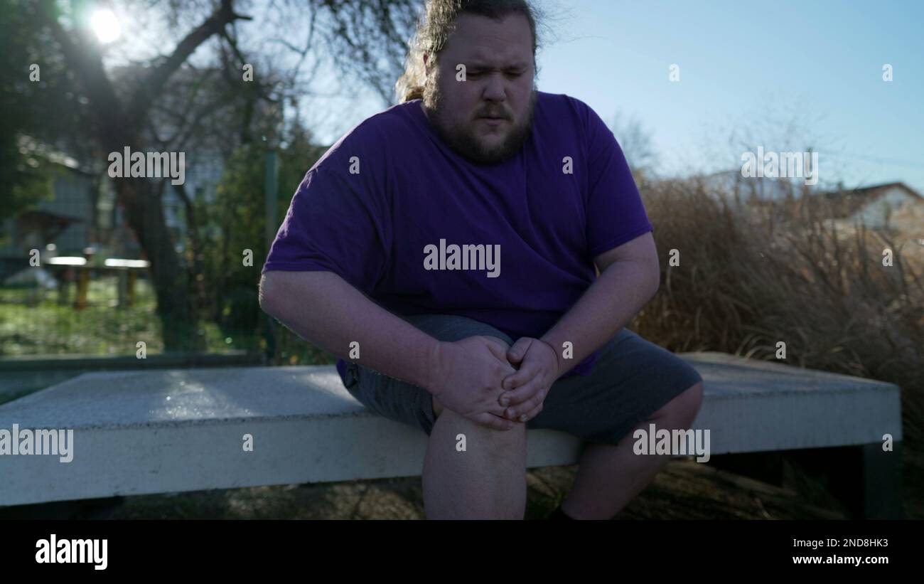Person suffering from knee pain sitting at bench outdoors. One ...