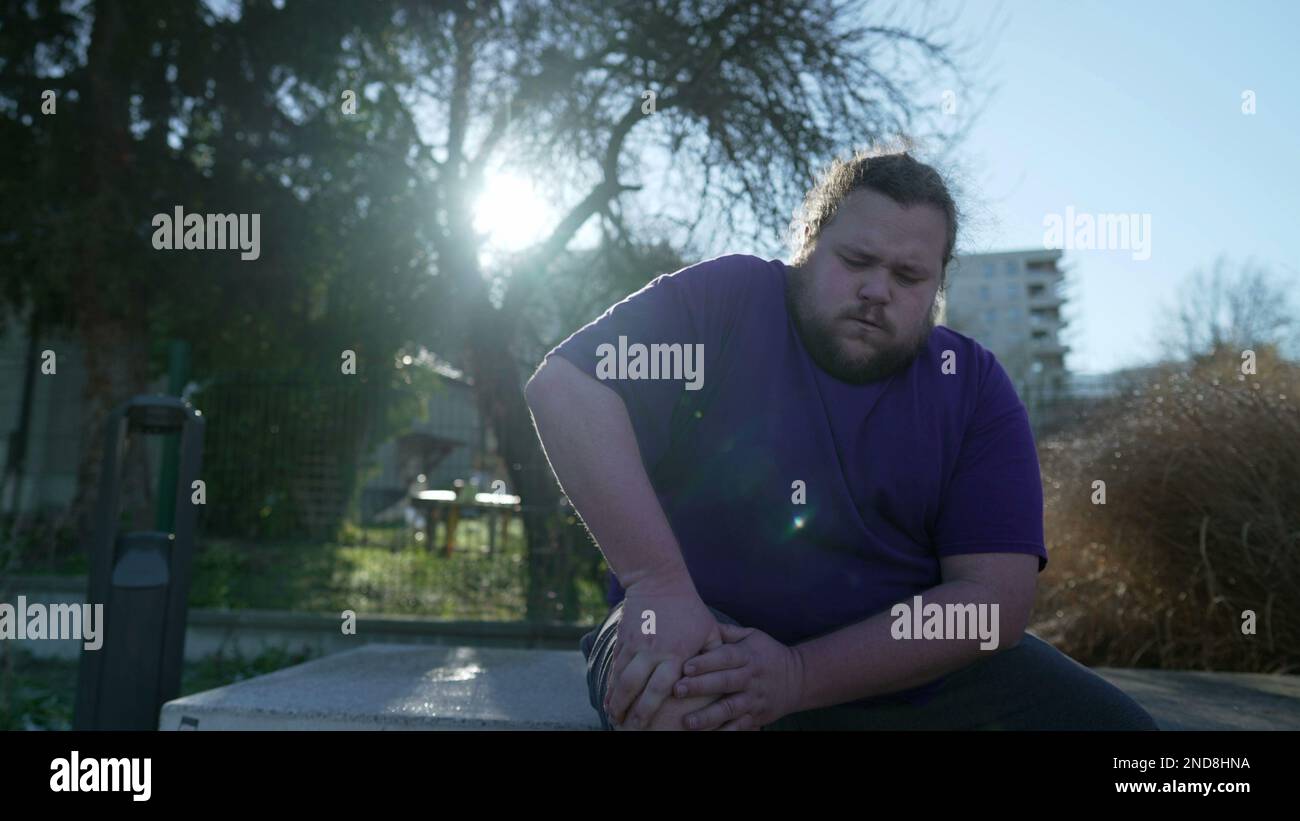 Person suffering from knee pain sitting at bench outdoors. One ...
