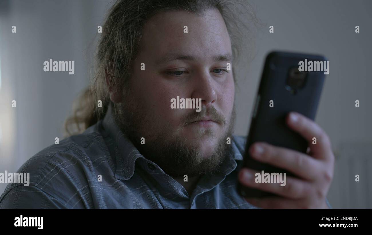 Close up young man looking at cellphone device. One overweight male ...