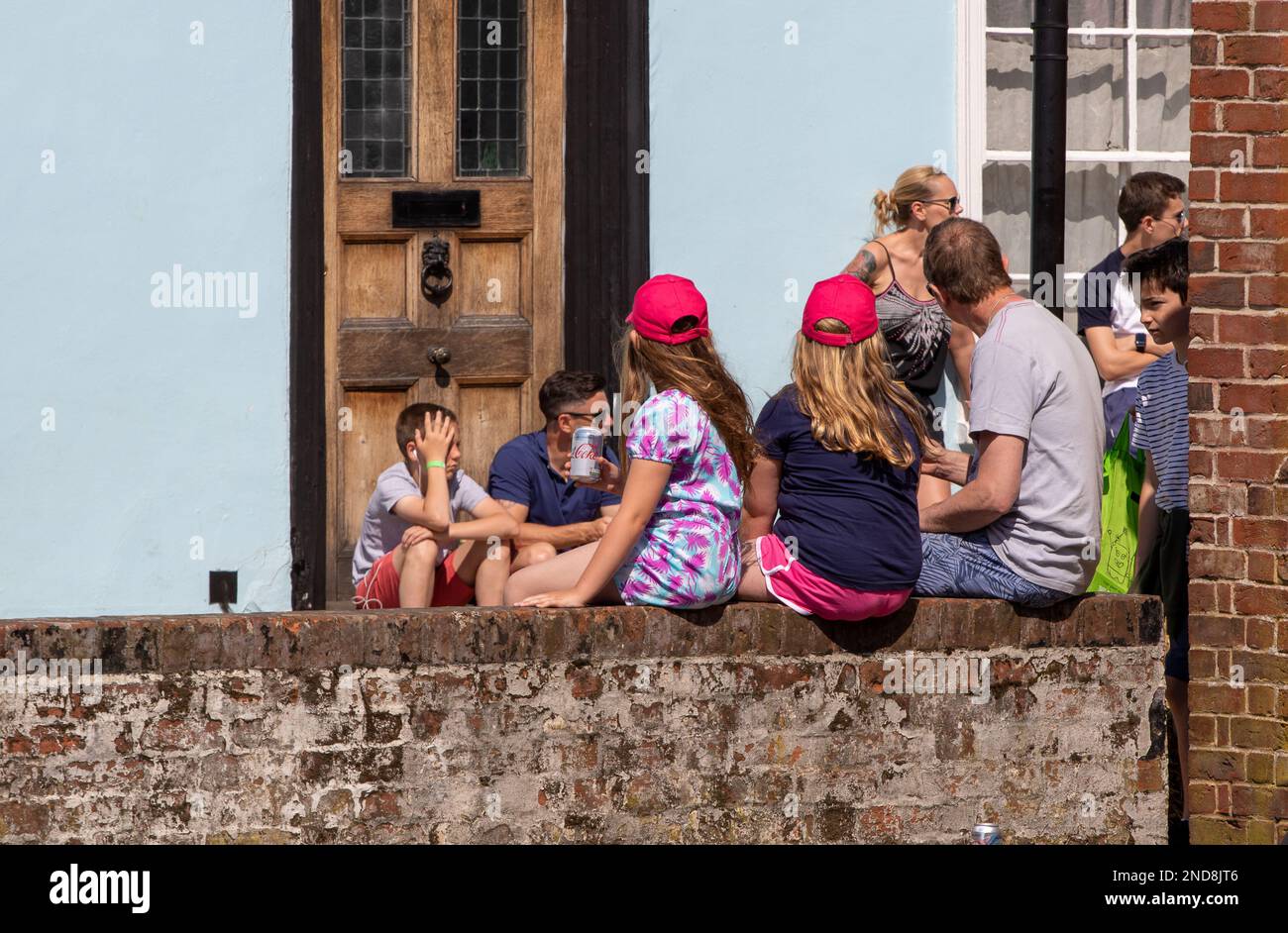 Two young girls in matching red baseball caps sit on a brick wall to ...