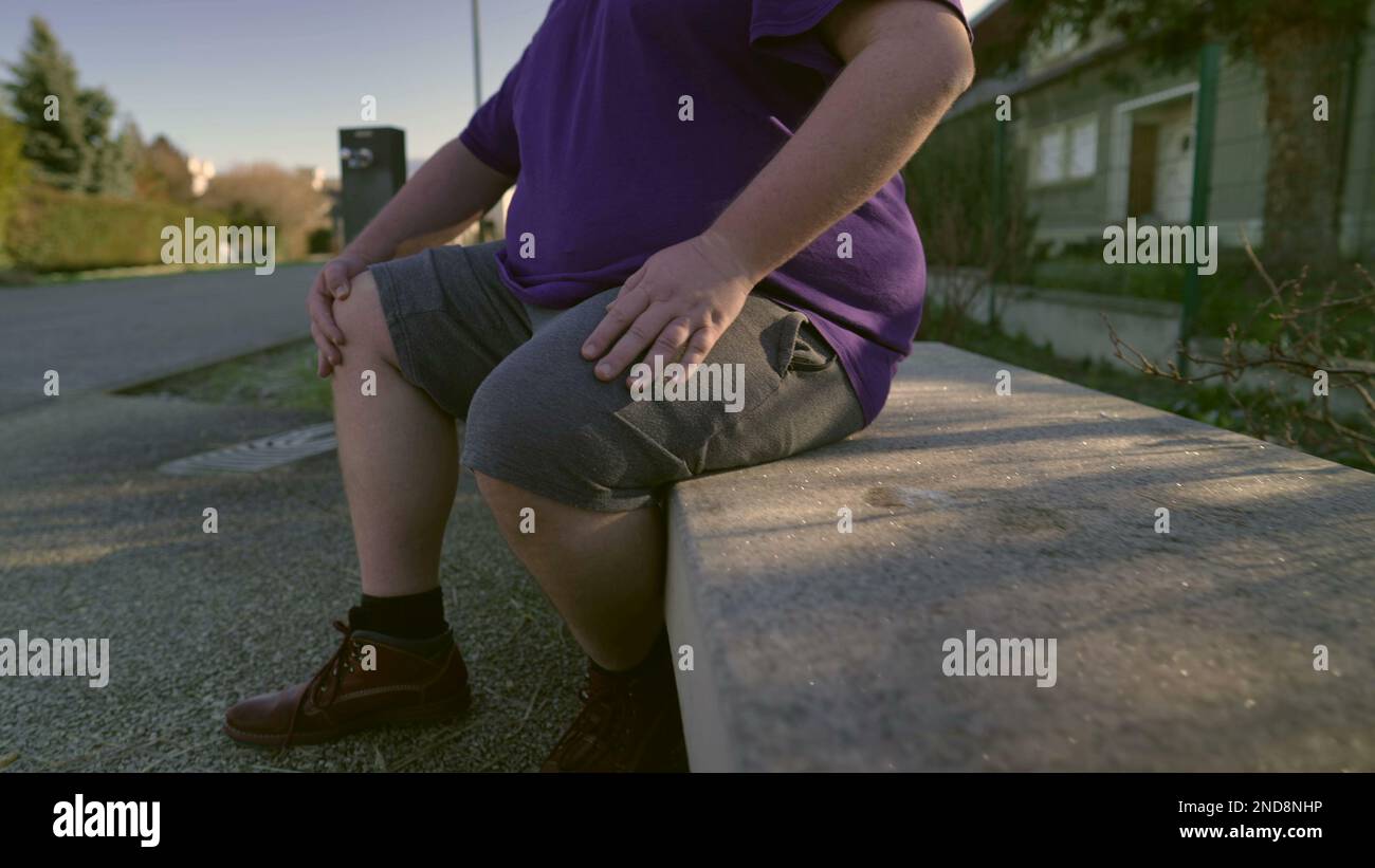 One tired young overweight man sitting down at park bench to rest. A ...