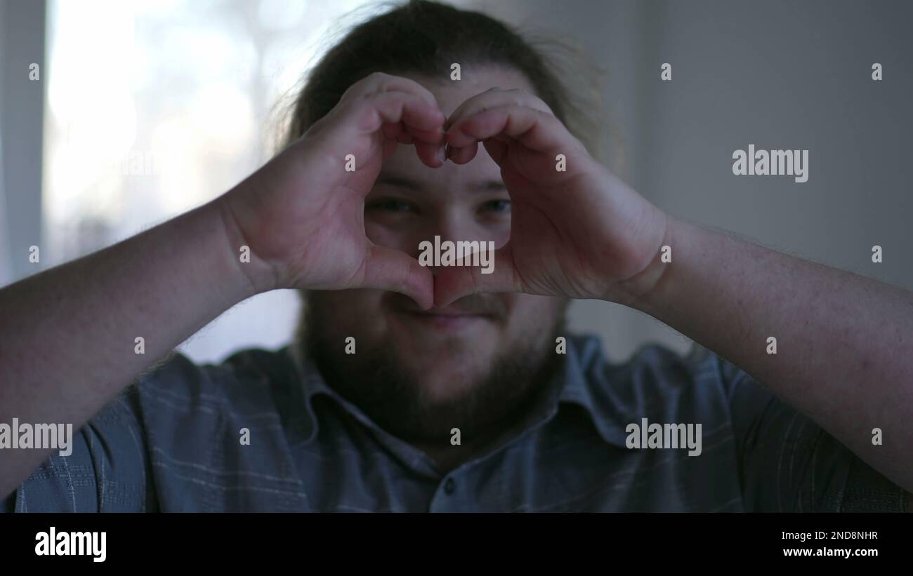 One young chubby man doing heart symbol with hands indoors. Happy ...