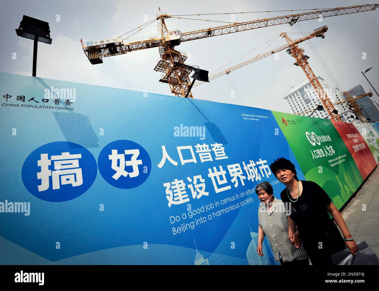 Chinese women walk past a roll of billboards featuring China population ...